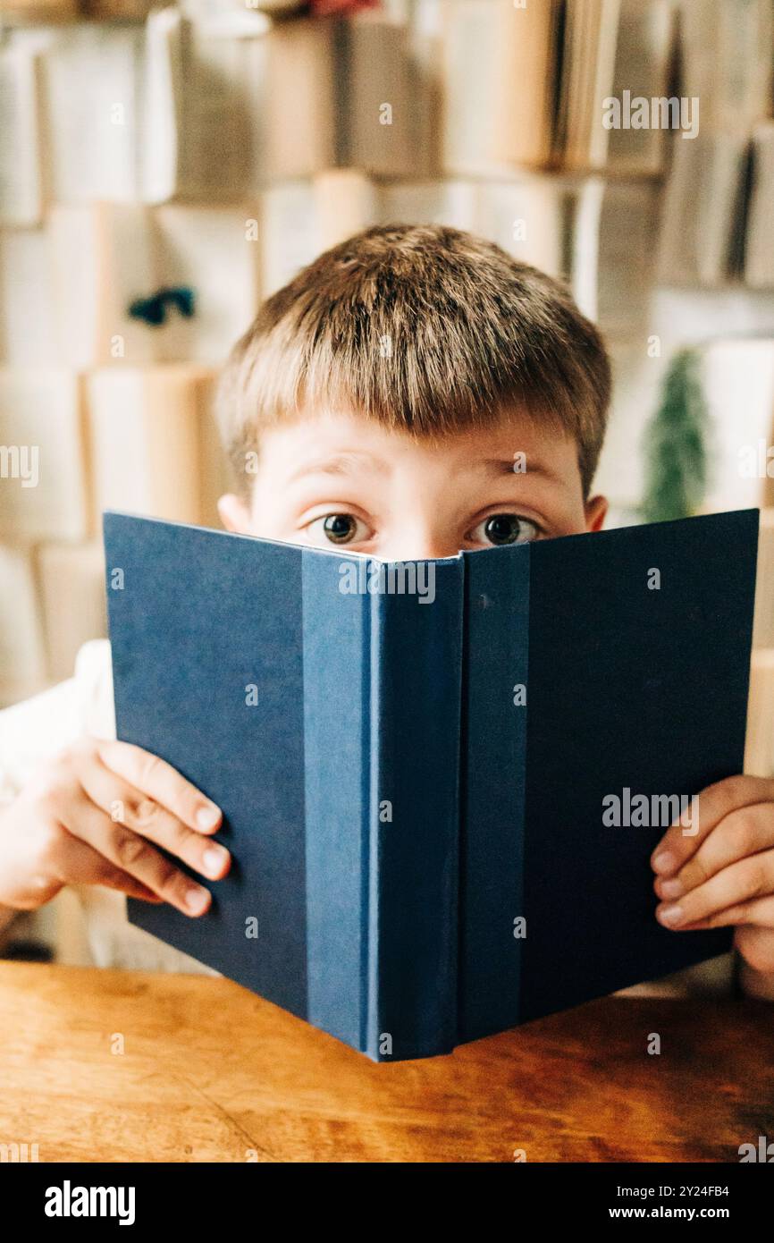 Boy peeking over a blue book with wide eyes, surrounded by books Stock ...