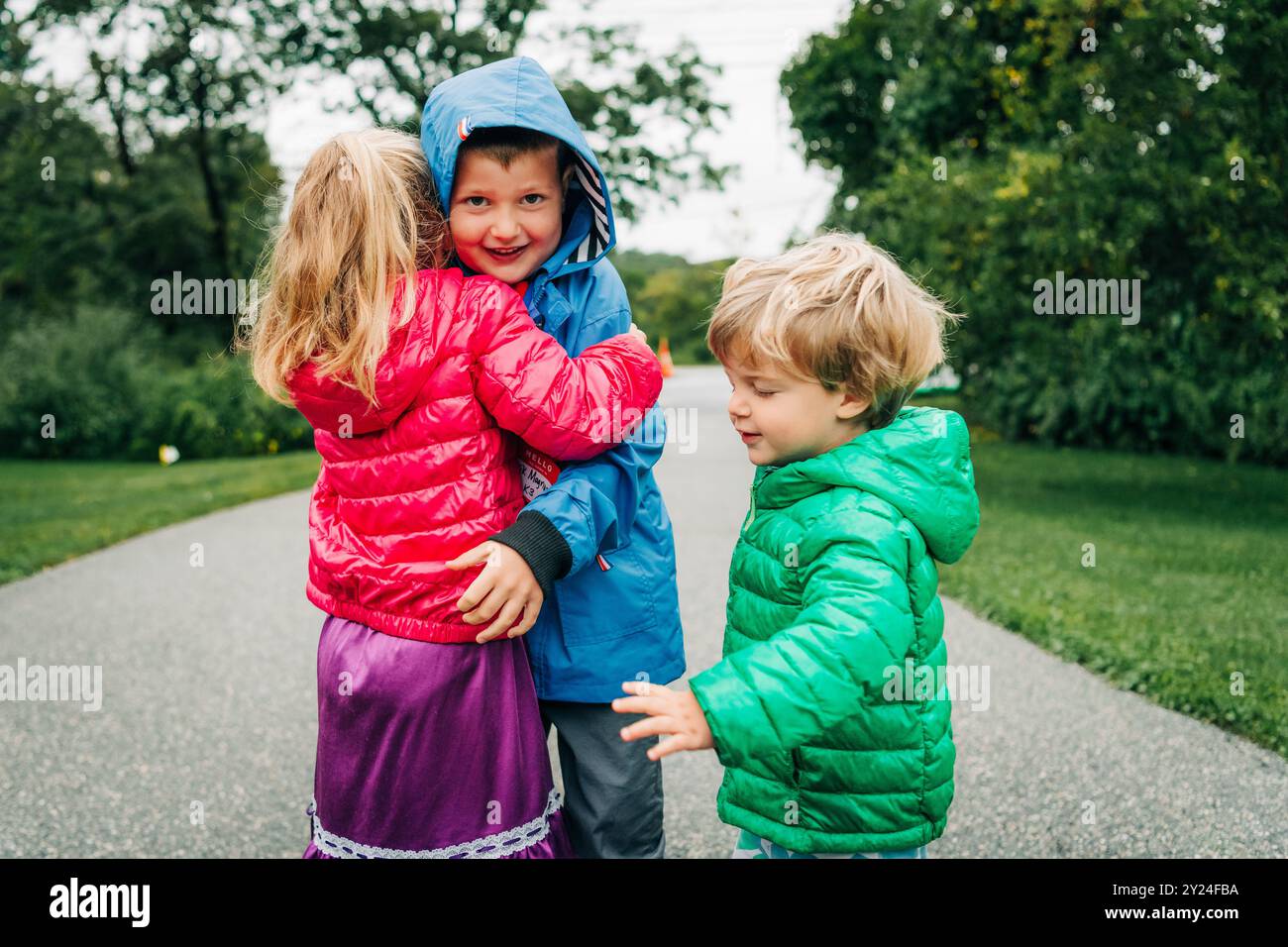 Three children hugging outdoors, dressed in bright jackets Stock Photo ...