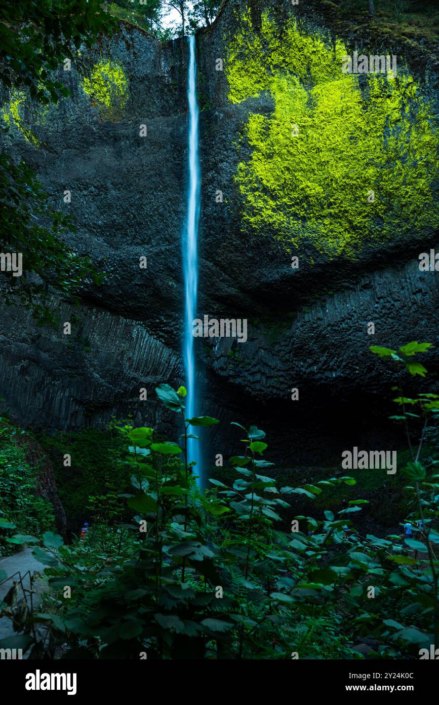 A tall waterfall drops from a rocky cliff covered in green moss Stock ...
