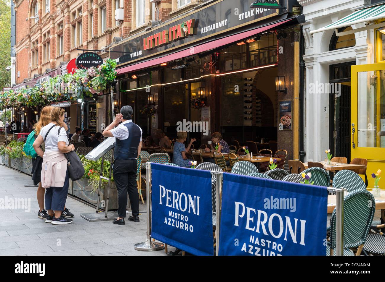 Two women in conversation with waiter maître d' at menu board outside ...