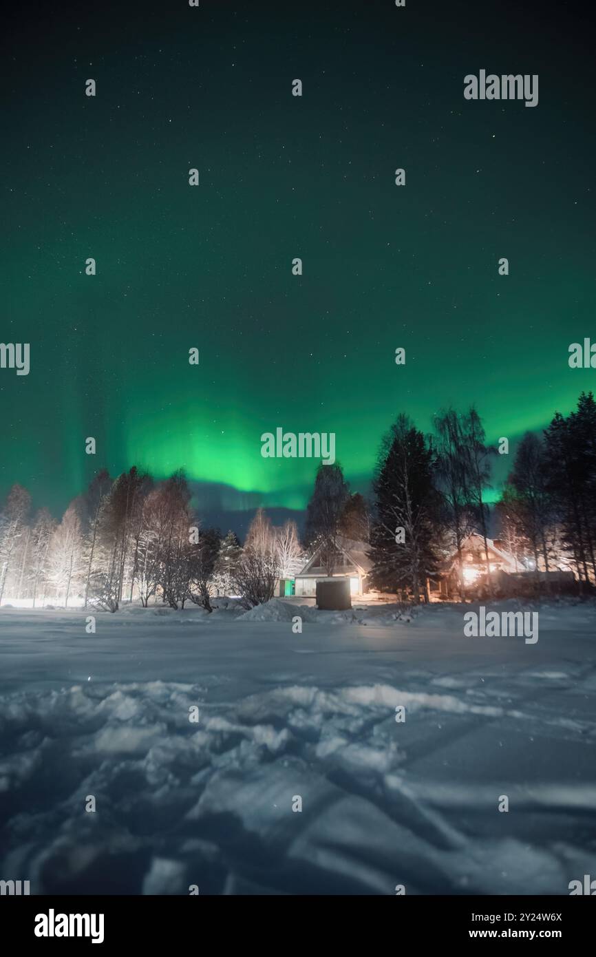 Strong green northern lights over house in snowy forest in Rovaniemi ...