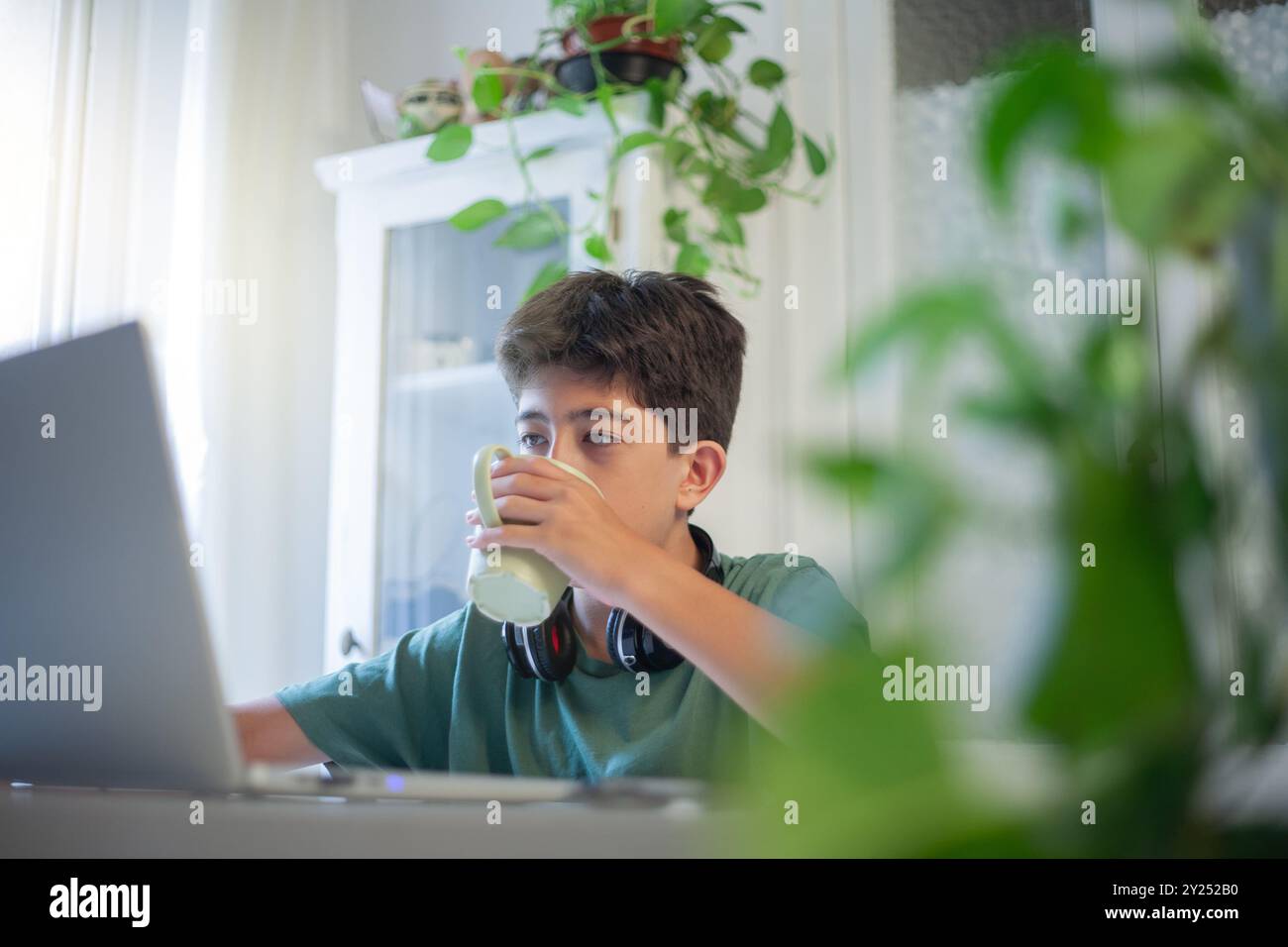 A boy drinks a hot beverage while using a laptop computer Stock Photo ...