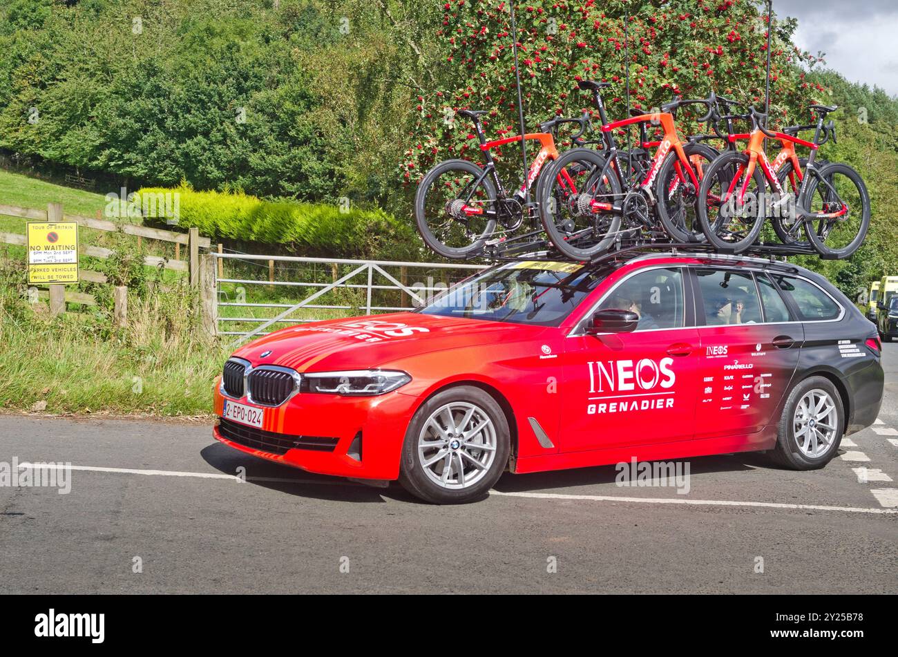 Ineos Grenadiers team car with riders' bikes on roof turning onto start ...