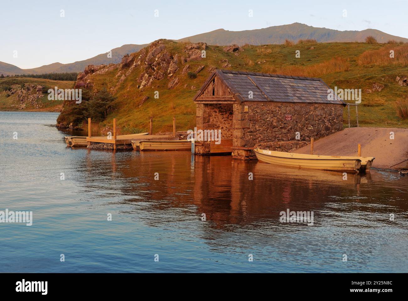 As the sun sets over Snowdon peak, the golden hour casts a warm glow on ...
