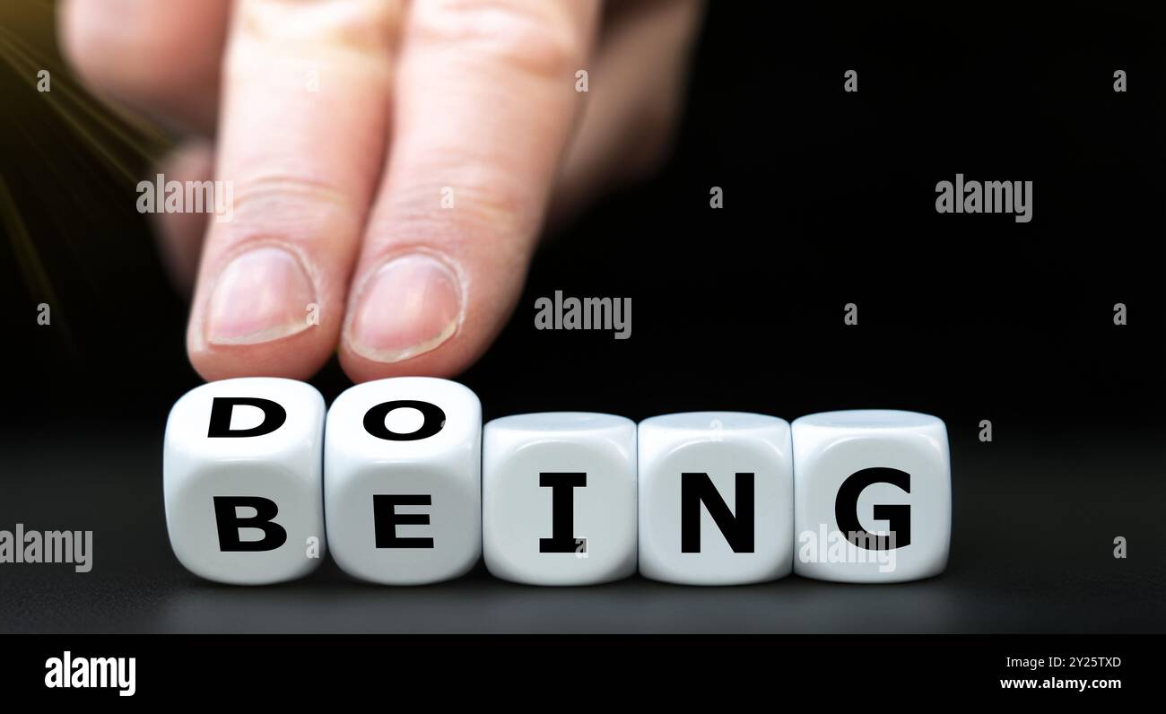 Hand turns dice and changes the word being to doing Stock Photo - Alamy