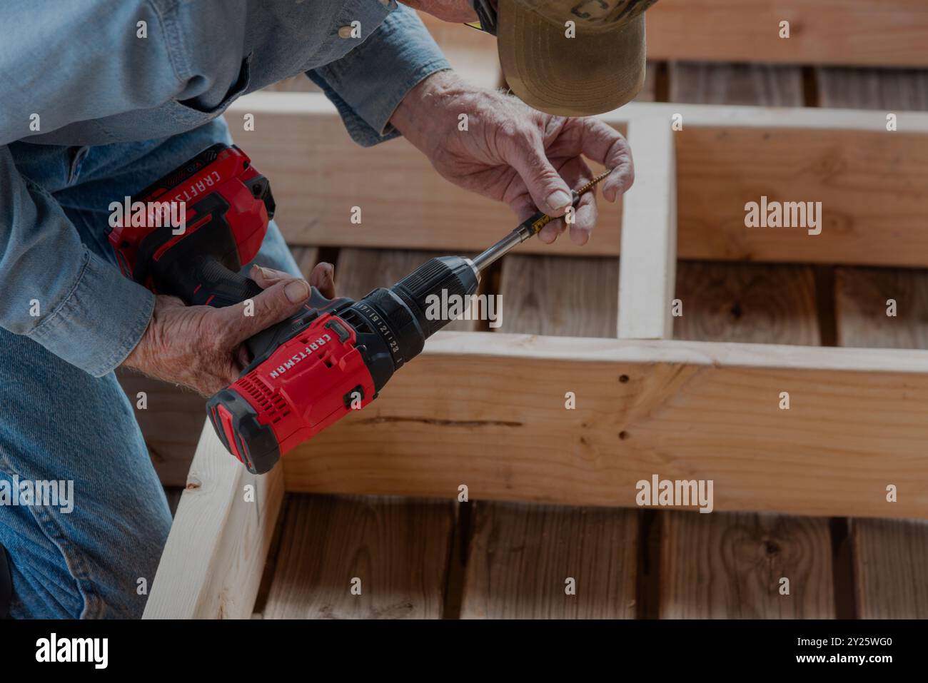 The hands of a man in his 80s on his knees bending over a framed wall ...