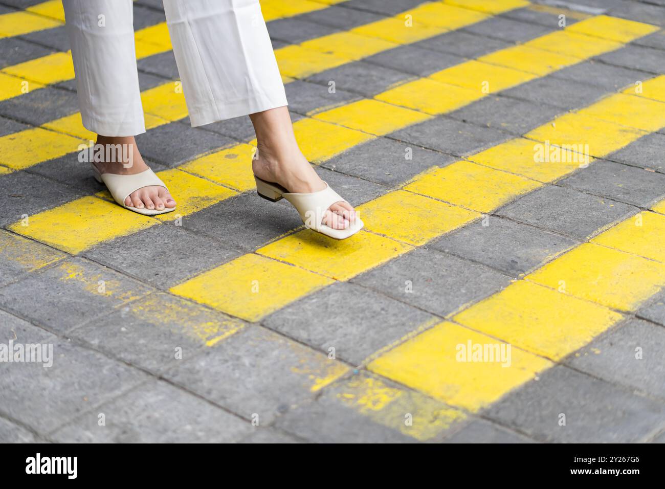 A close-up of a woman's foot wearing stylish white sandals stepping on ...
