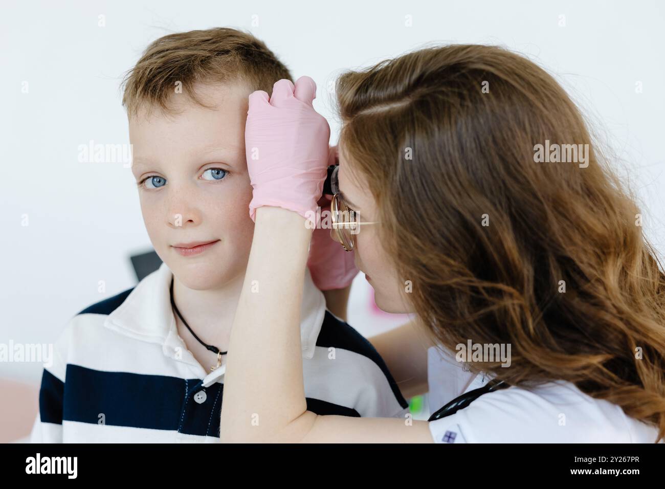 Female doctor examining boy's ear with otoscope in office. Ear cavity ...