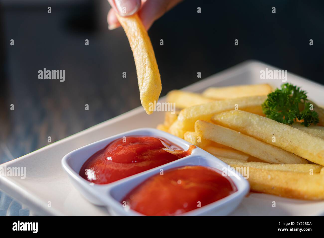 A close-up of a hand holding a French fry above two small bowls of ...