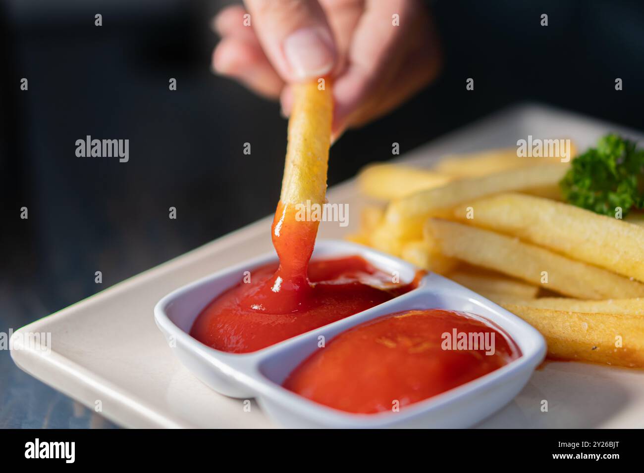 A close-up of a hand holding a French fry above two small bowls of ...