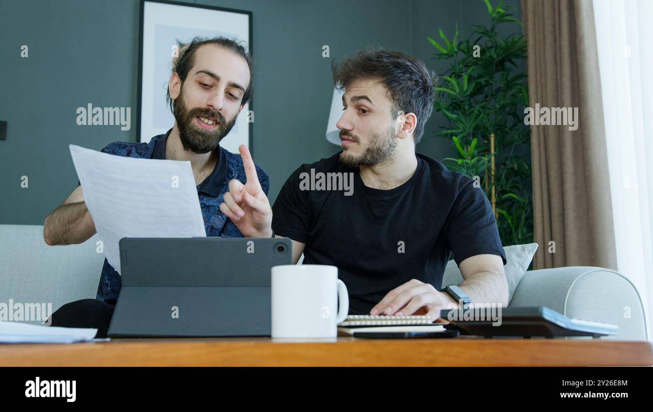 Two men are sitting on a couch, engaged in a project discussion. The ...