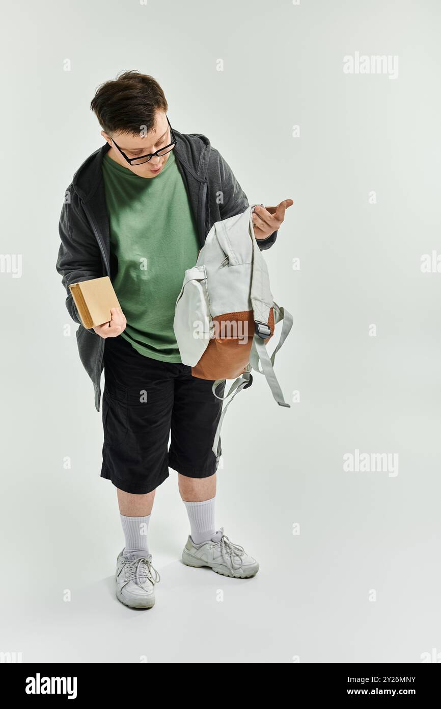 A young man with Down syndrome explores his backpack and holds a book ...