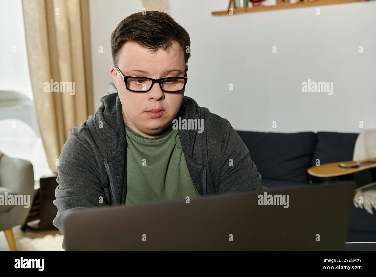A young man with Down syndrome engages with his laptop in a cozy home ...