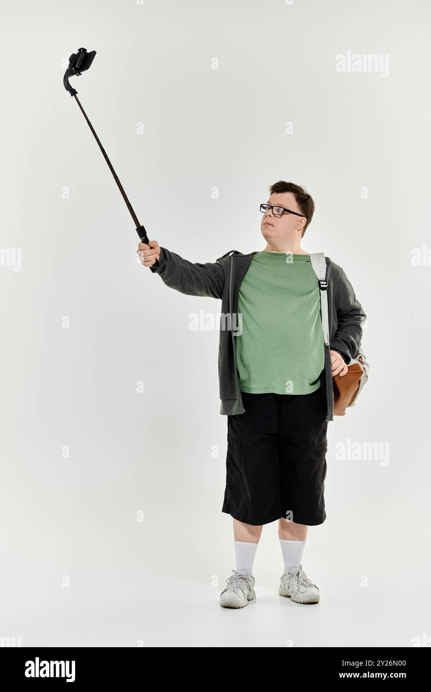 A young man with Down syndrome stands confidently taking a selfie with ...
