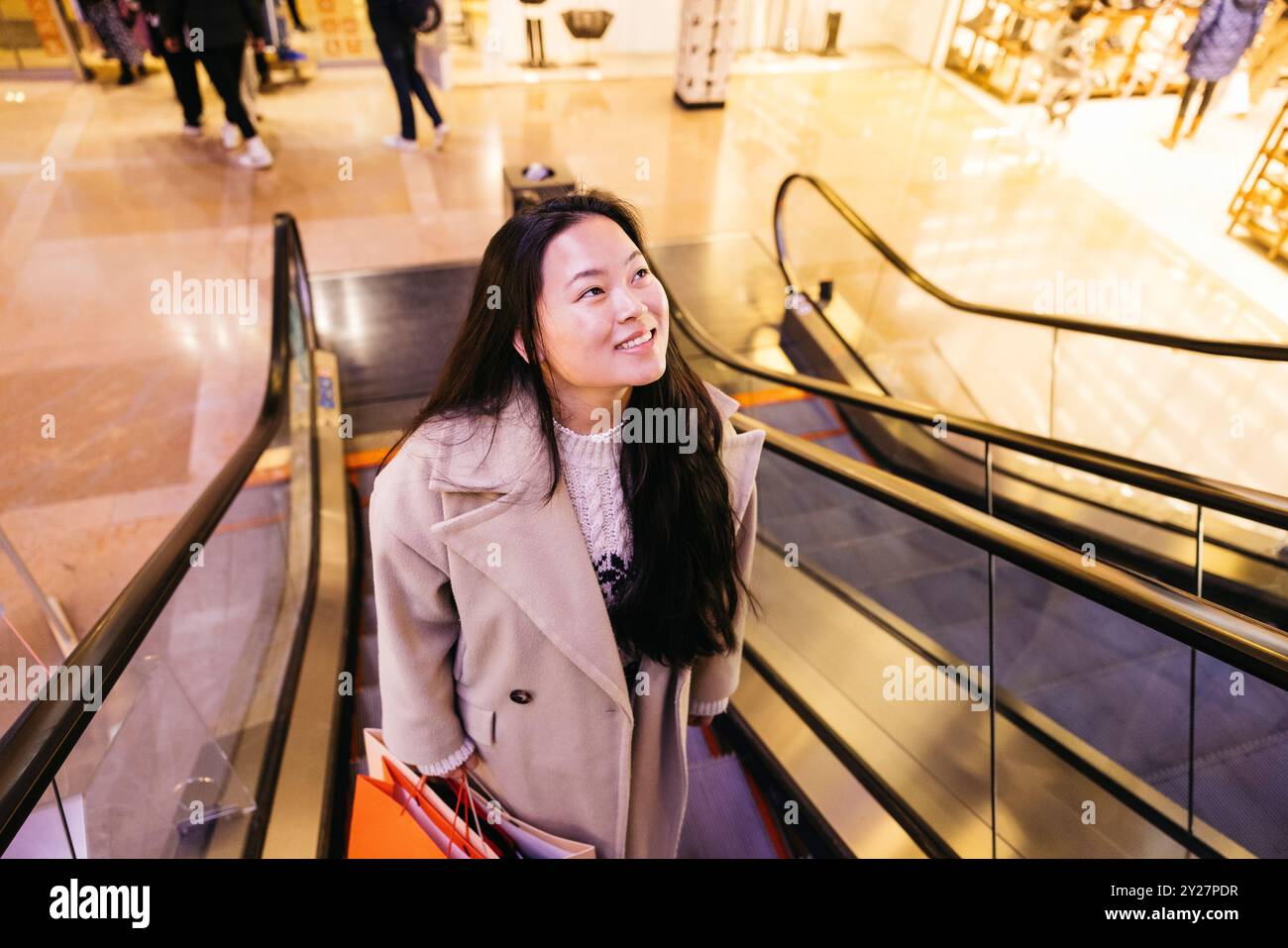 Young smiling Asian woman riding an escalator in a shopping mall ...