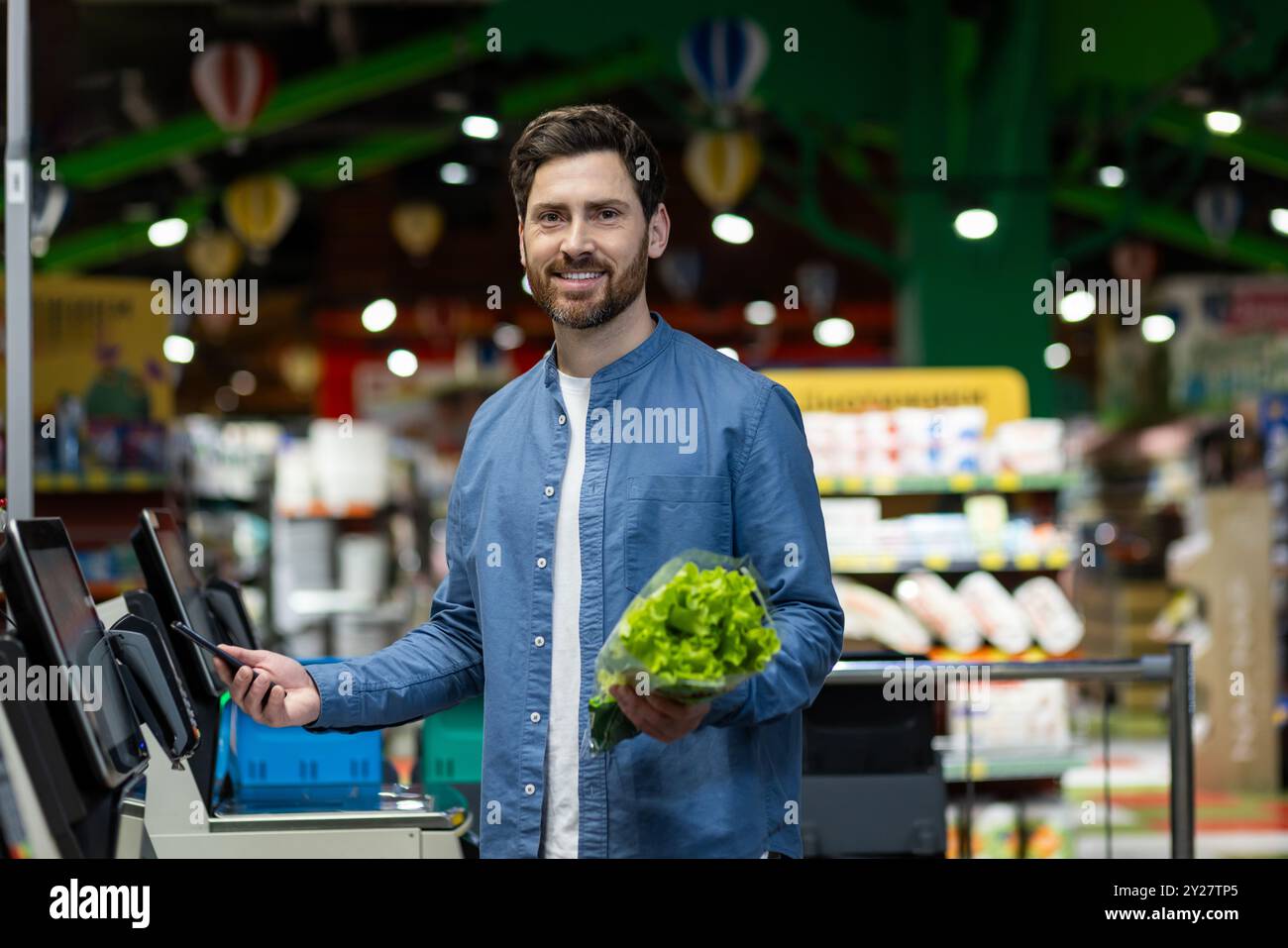 Young man using phone at self-checkout kiosk in grocery store. Person ...