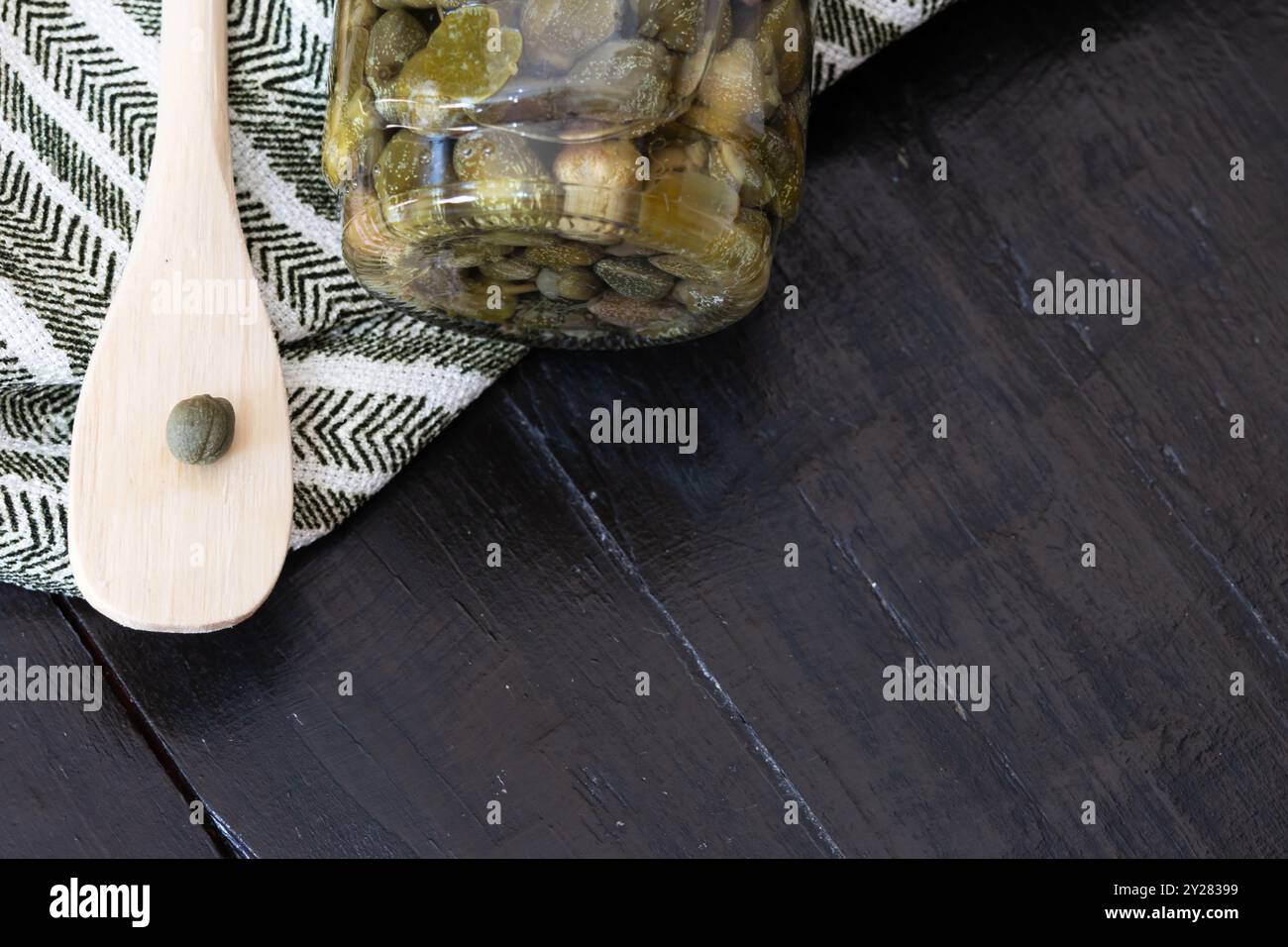 Image composed of a caper on top of a spoon and part of a jar of ...