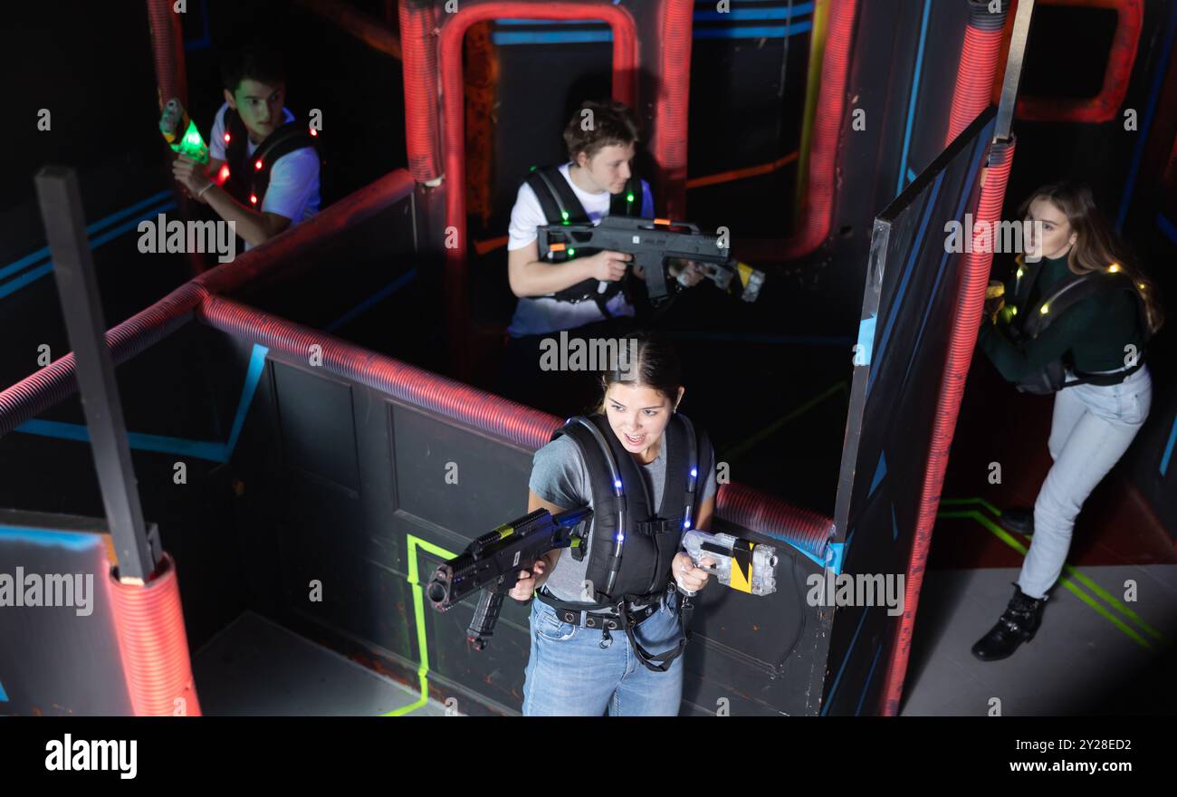 Four people having fun playing lasertag ducking behind cover in maze of ...