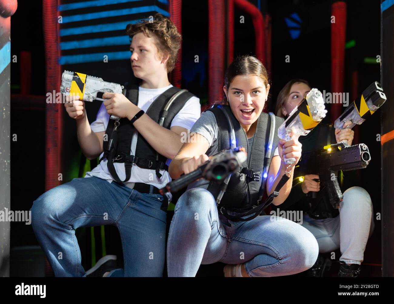 Modern young people with laser pistols playing laser tag on dark ...