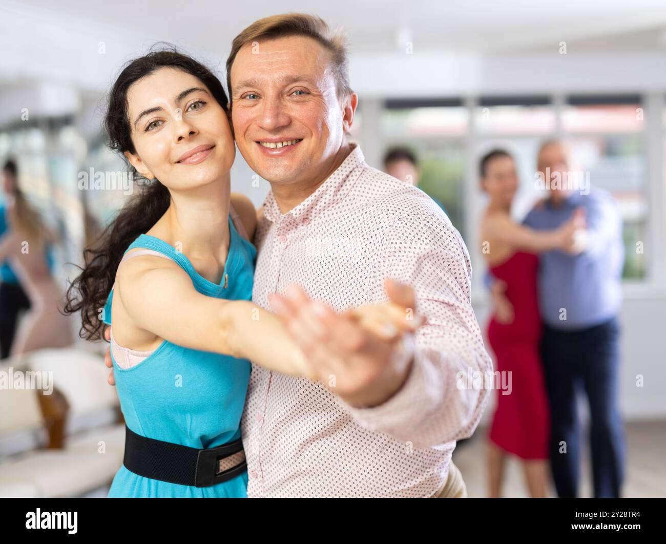 Happy people of different ages dancing tango in pairs in dance hall ...
