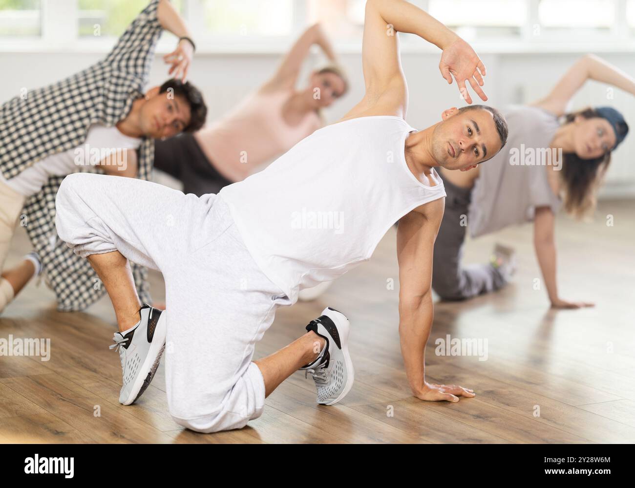 Man and his students perform hip hop dance on one bent leg, movement in ...