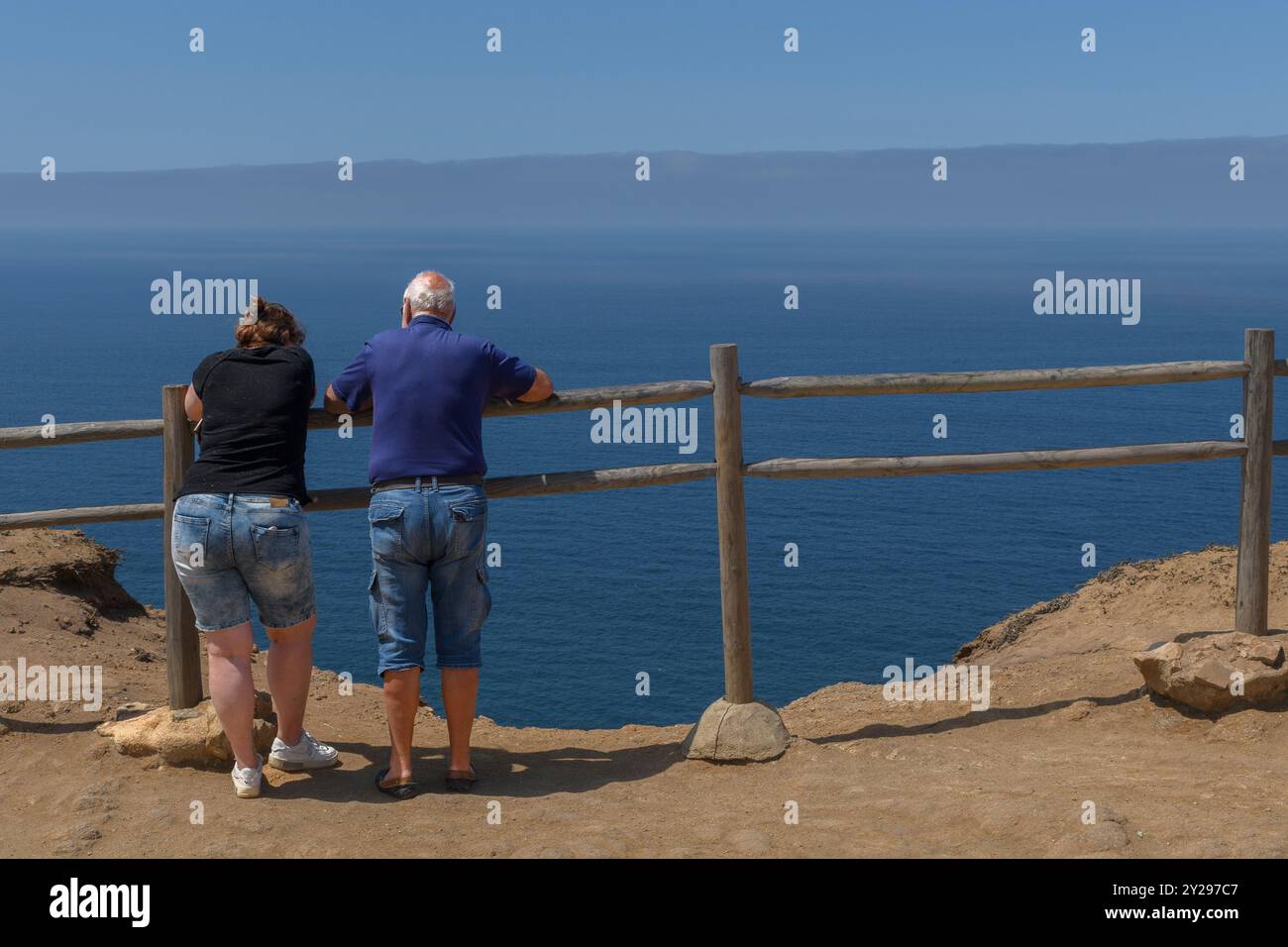 Man and woman leaning on a wooden railing looking out from the cliff at ...