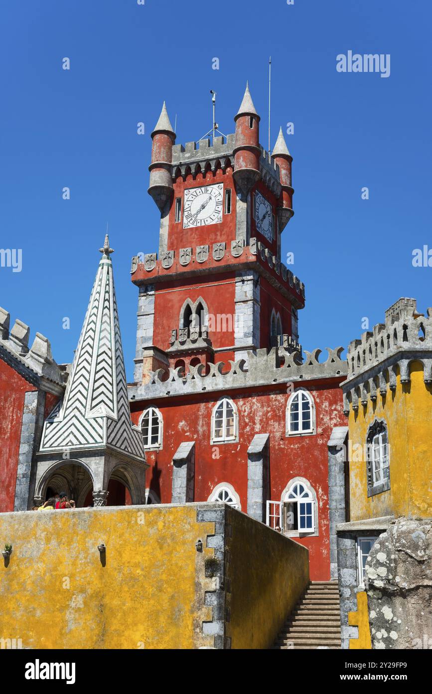 Red tower with clock and yellow facade, pointed roof and blue sky ...