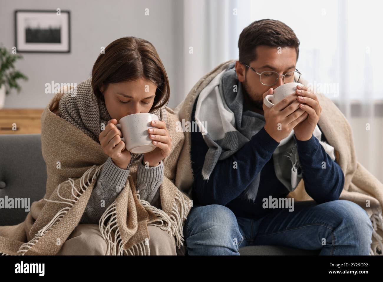 Cold symptom. Couple with cups of drink suffering from fever on sofa at ...