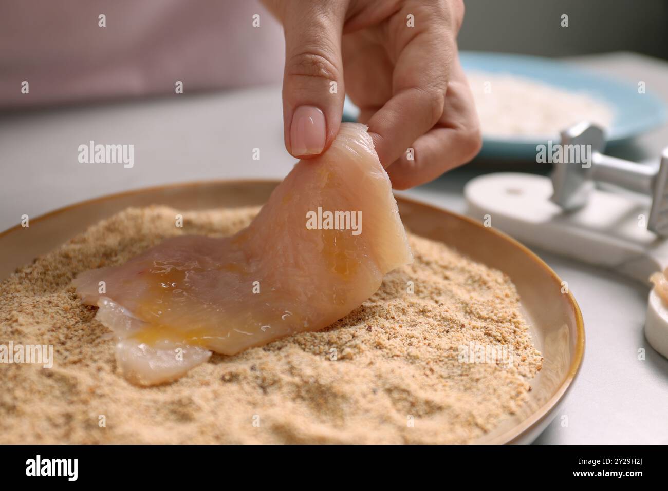 Making schnitzel. Woman coating slice of meat with bread crumbs at grey ...