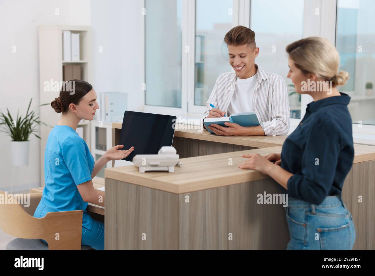 Professional receptionist working with patients at wooden desk in ...