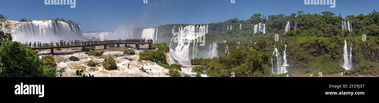 Panorama of spectacular Iguazu Falls with visitor platform and blue sky ...