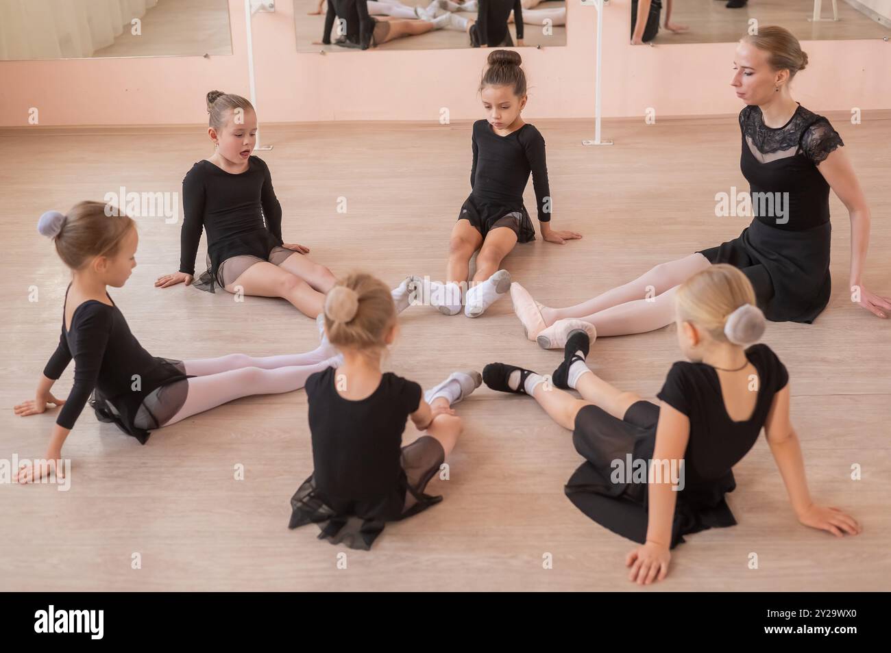 Caucasian woman and five little girls sit in a circle and do stretching ...