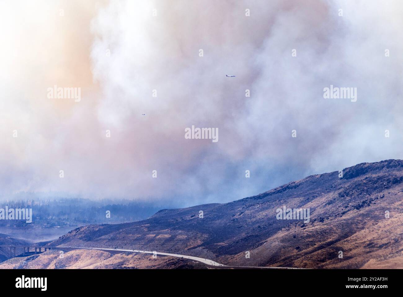 Firefighting planes fly through heavy smoke shadowing the land below ...