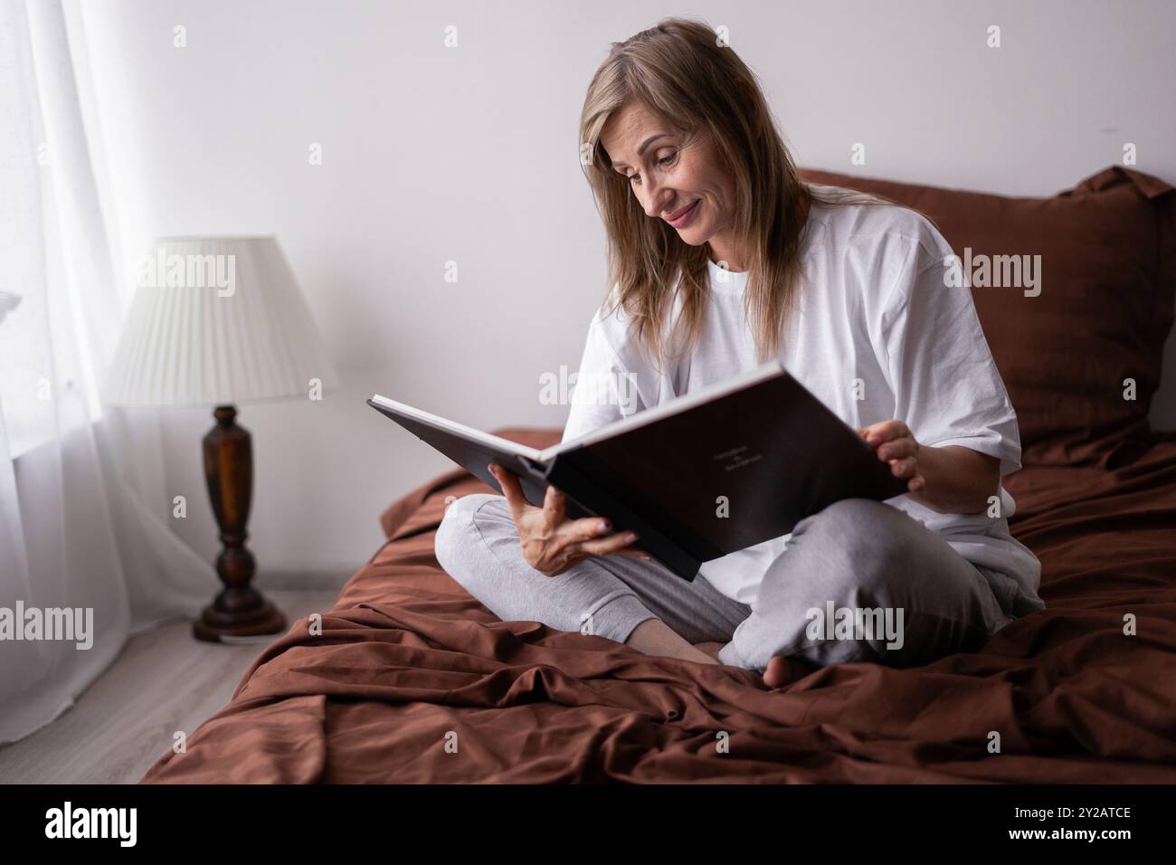 Middle aged woman looking at photo album while sitting on bed Stock ...