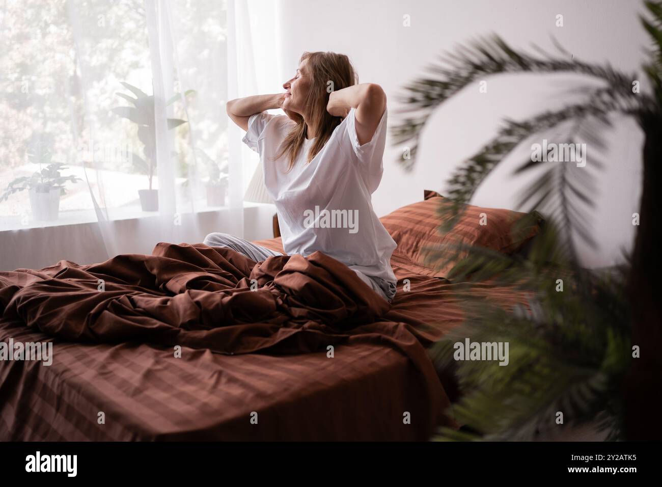 Elderly woman waking up in morning, sits on her bed and stretches after ...