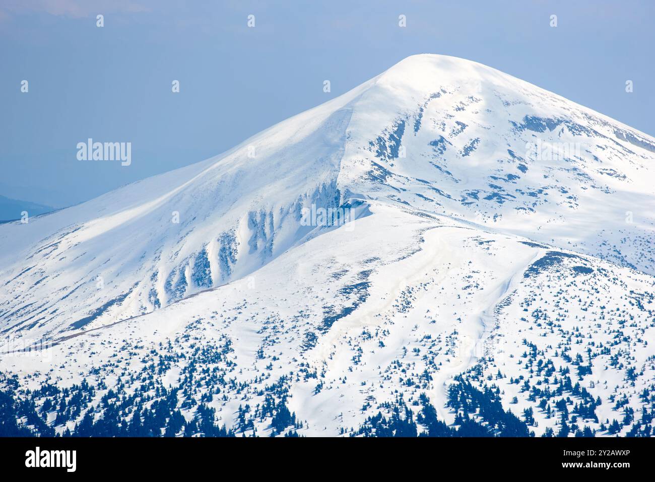 Snow-covered mountain peak under clear blue sky, with patches of snow ...