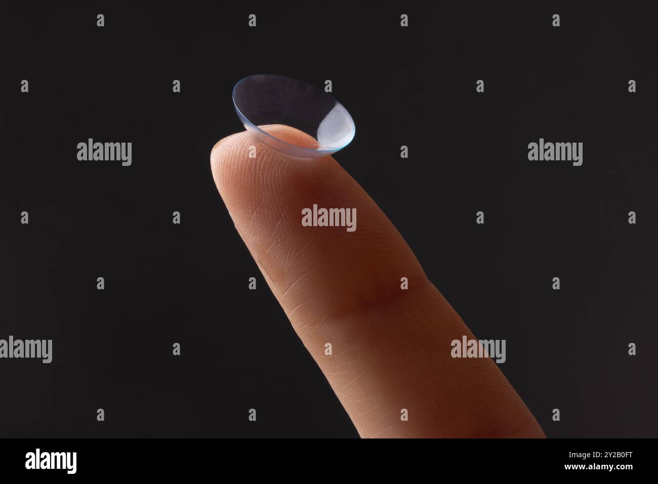 Close-up of finger holding contact lens, on grey background, concept of ...