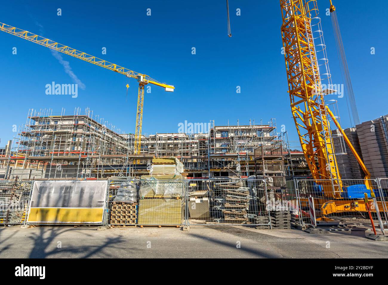 Construction site with cranes, scaffolding, fence and unfinished ...