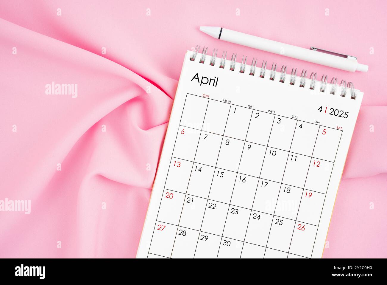 April 2025 month calendar and pen on pink fabric background. Monthly ...