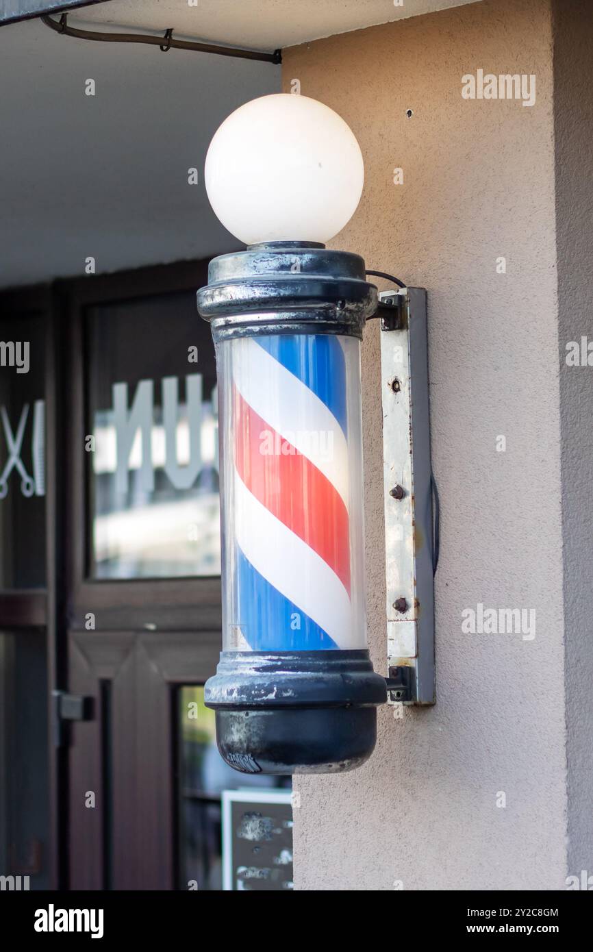 A red, white, and blue barber pole is mounted on the exterior wall of a ...
