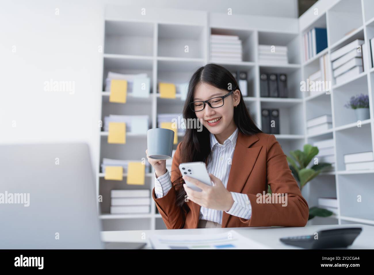A businesswoman takes a break from her financial tasks, relaxing with a cup of coffee to ...