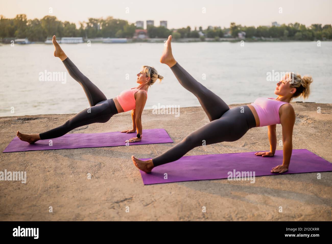 Two women practicing pilates outdoor in the city. Leg pull back ...