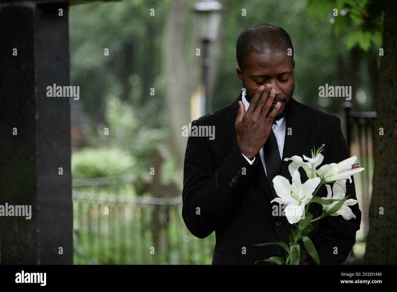 Medium shot of African American man in funeral black suit grieving at ...