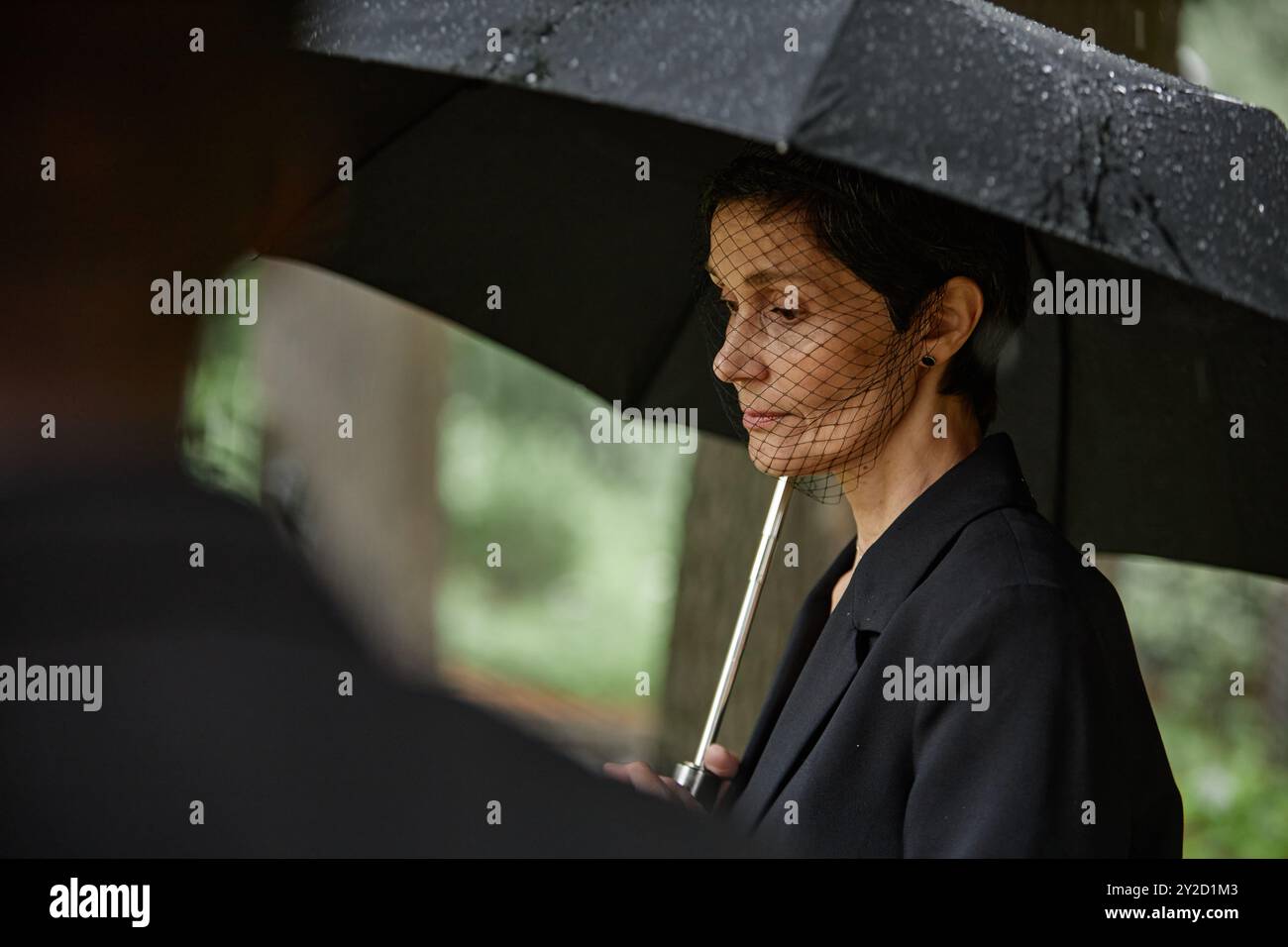 Side view of senior woman in black suit and veil grieving over loss of ...