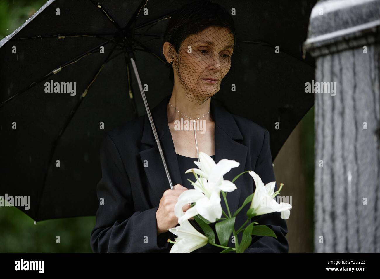 Medium shot of senior woman in mourning veil holding white lilies ...