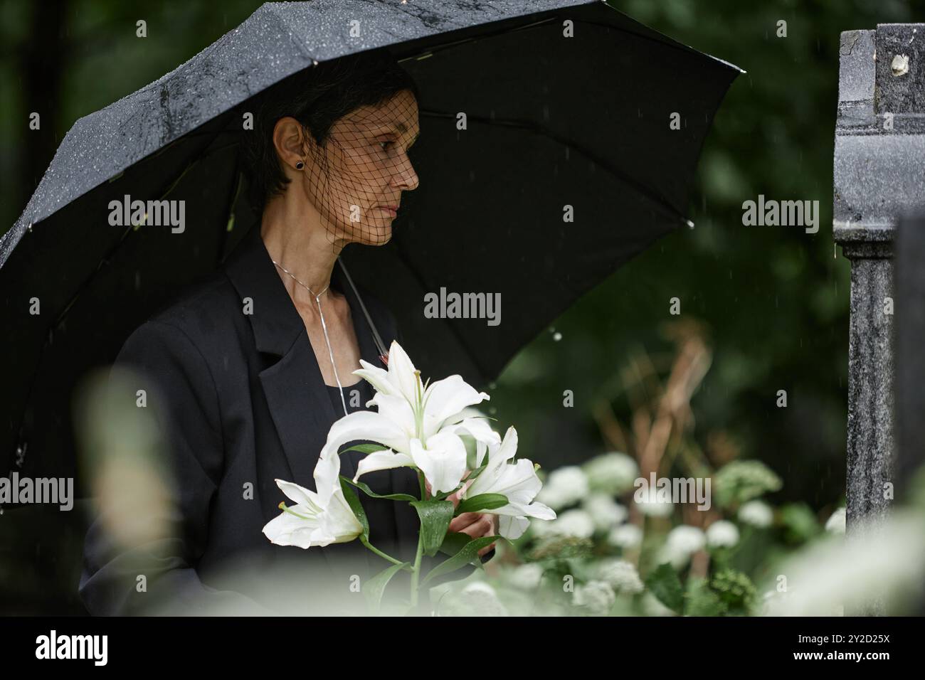 Side view of senior woman in mourning veil grieving next to grave with ...