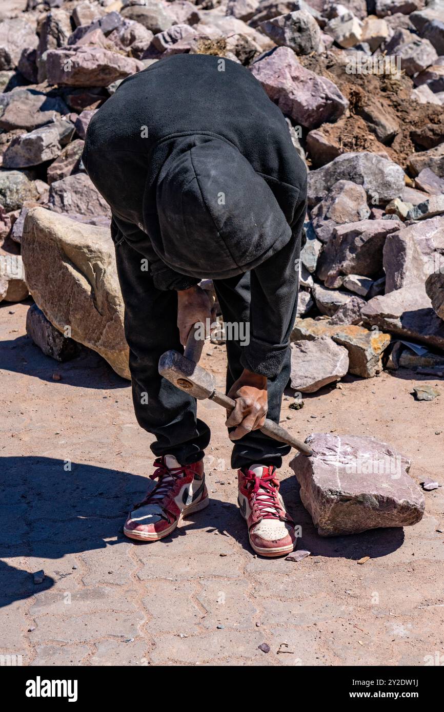 A stone mason shapes a stone with a hammer and chisel at a construction ...