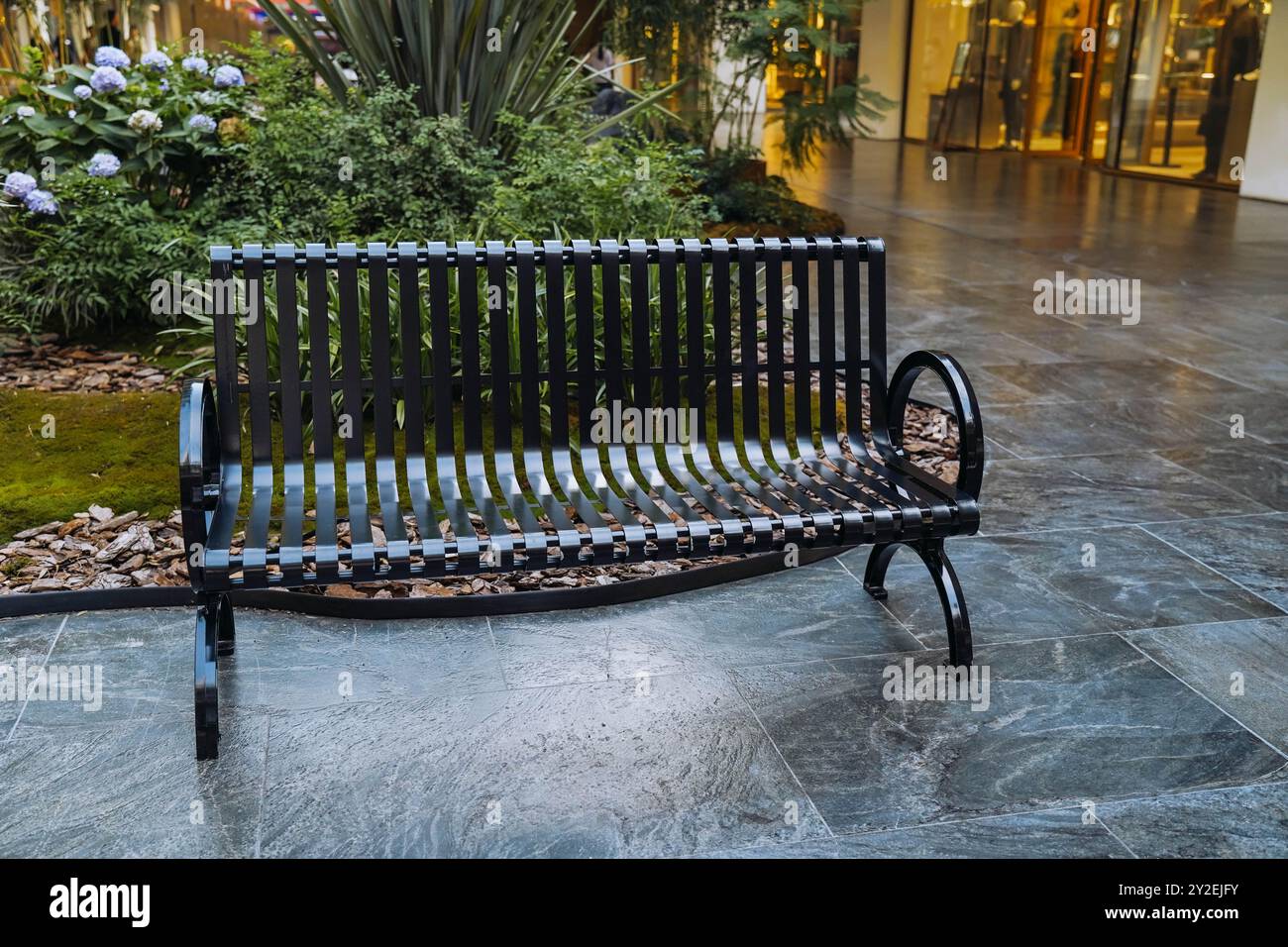 A wrought iron bench is placed in shopping mall for people to sit and ...