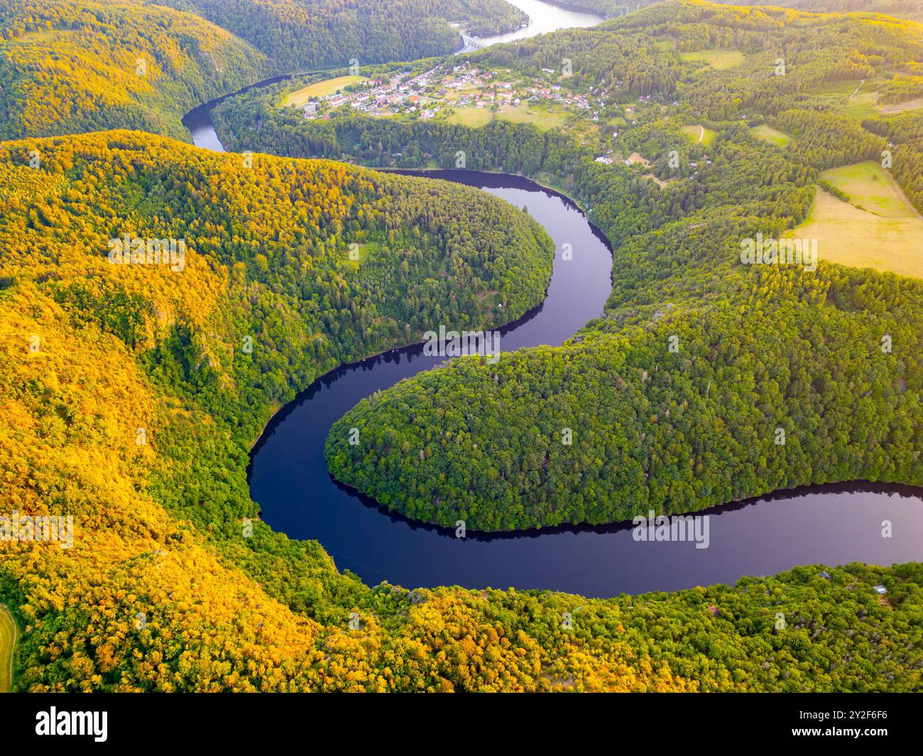 The vibrant sunset casts a warm glow over the winding Vltava River ...