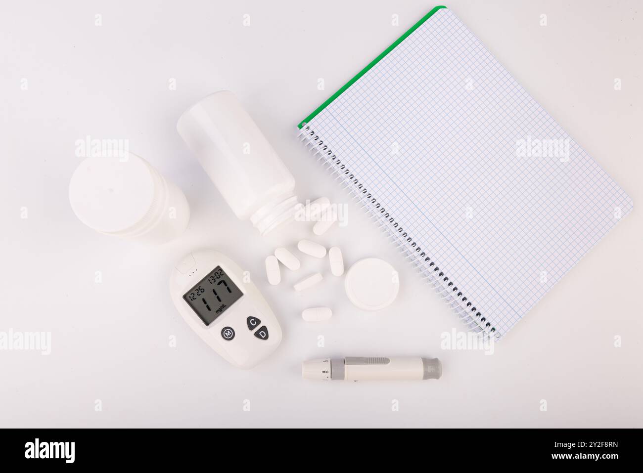 A top-down view of a glucose meter, a notebook, and white pills on a ...